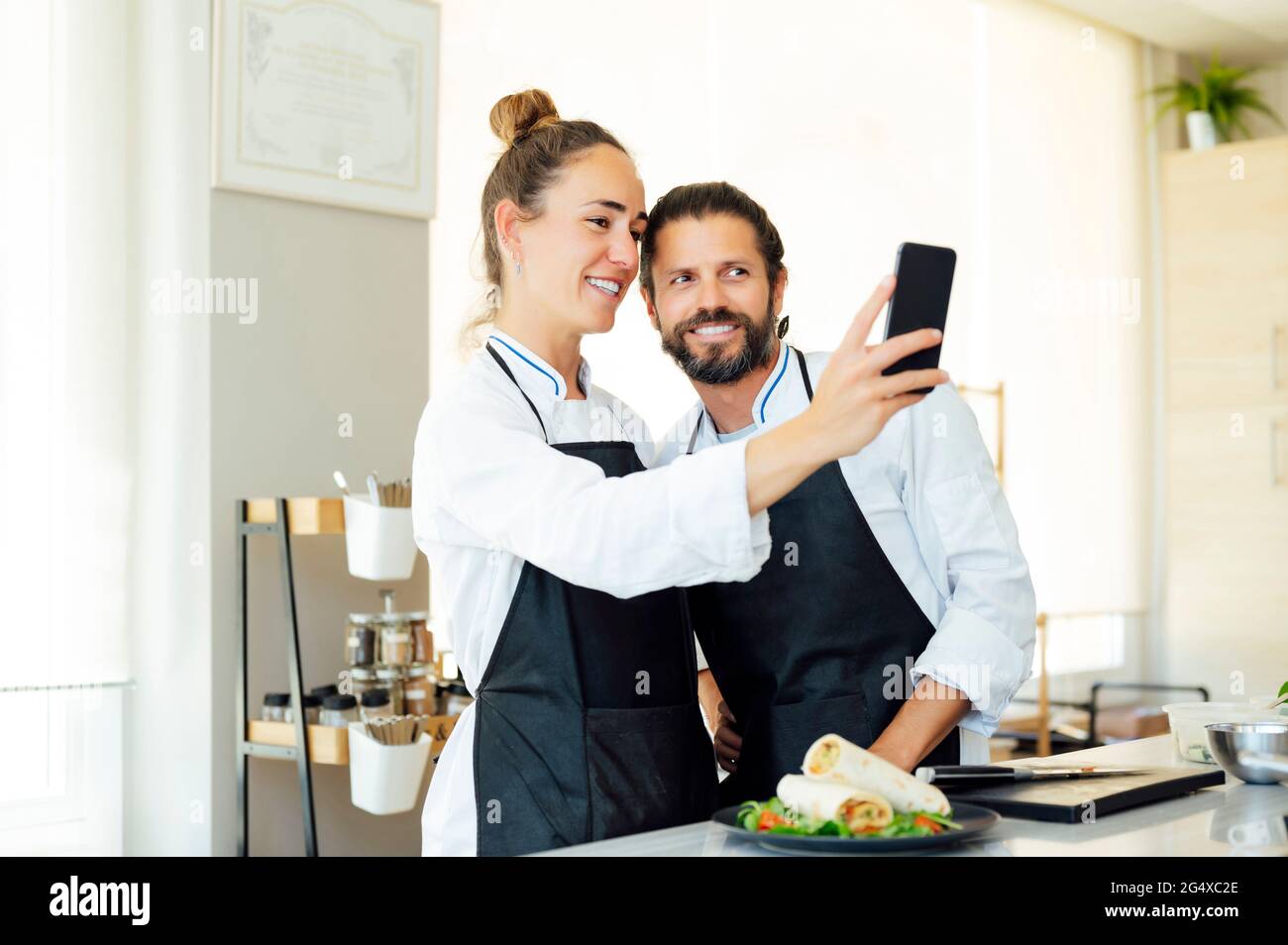 Happy chefs taking selfie with mobile phone in kitchen of modern ...