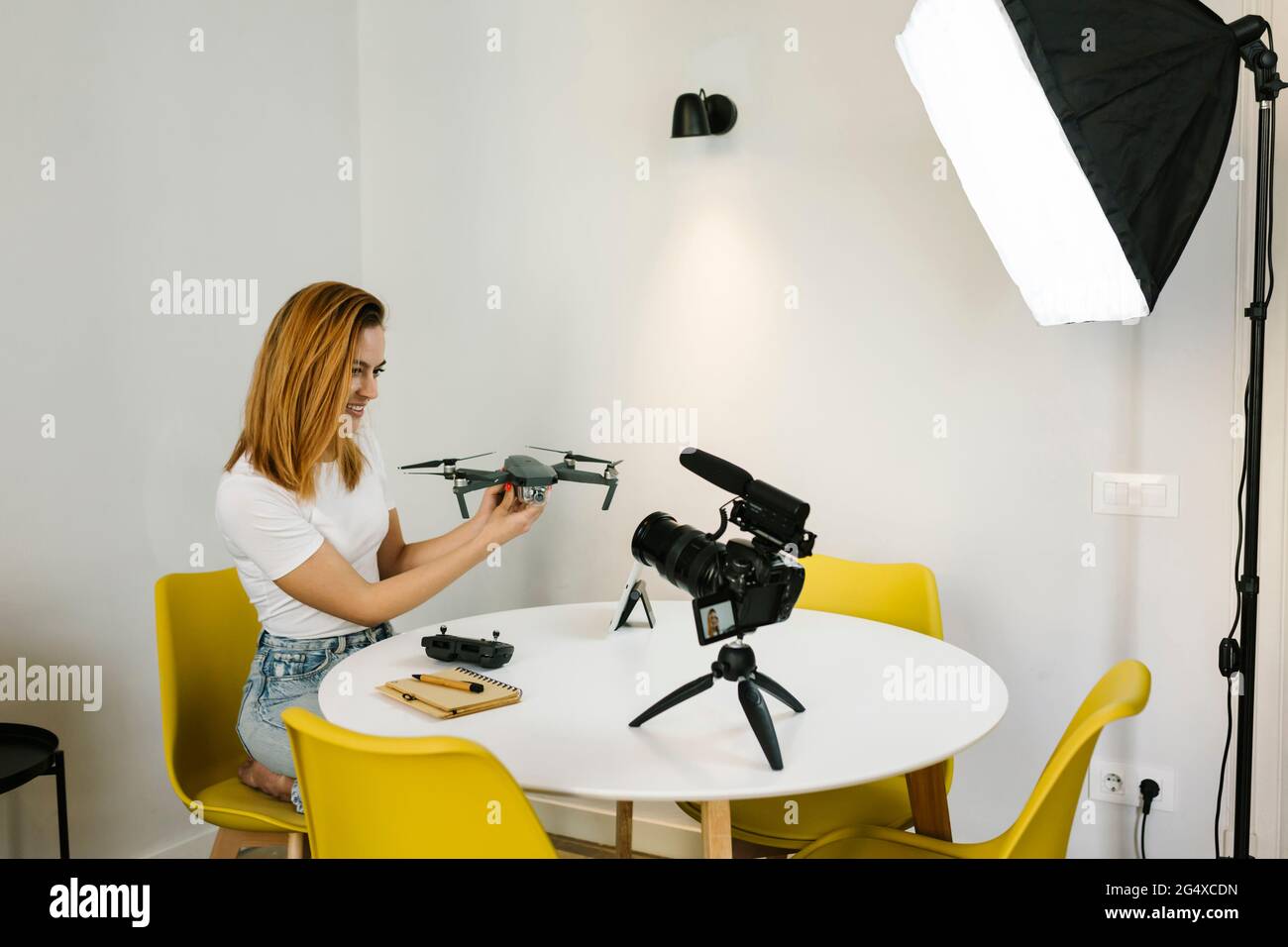 Smiling female influencer with drone vlogging by wall at home Stock ...