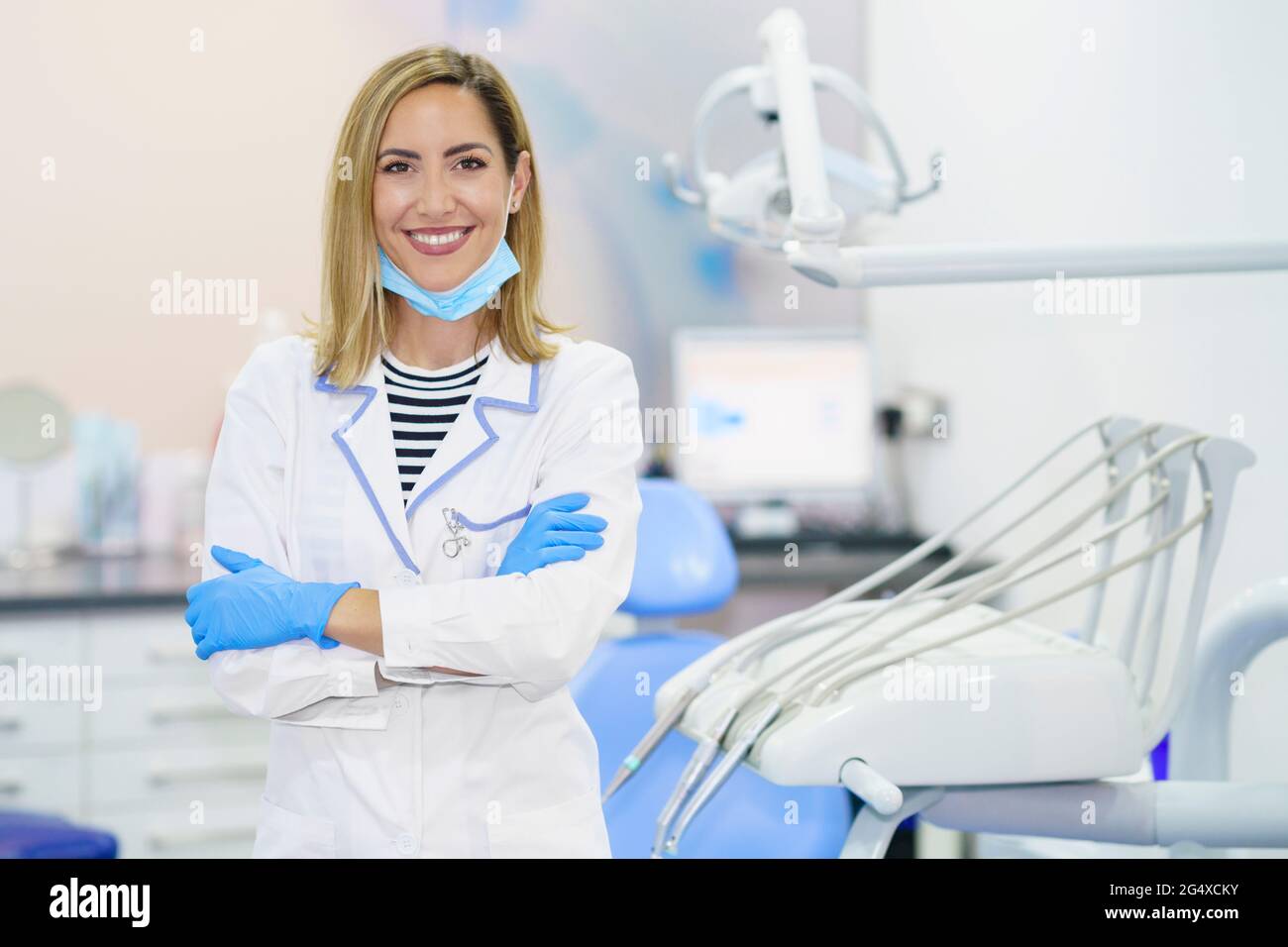 Smiling female dentist with arms crossed standing at medical clinic ...