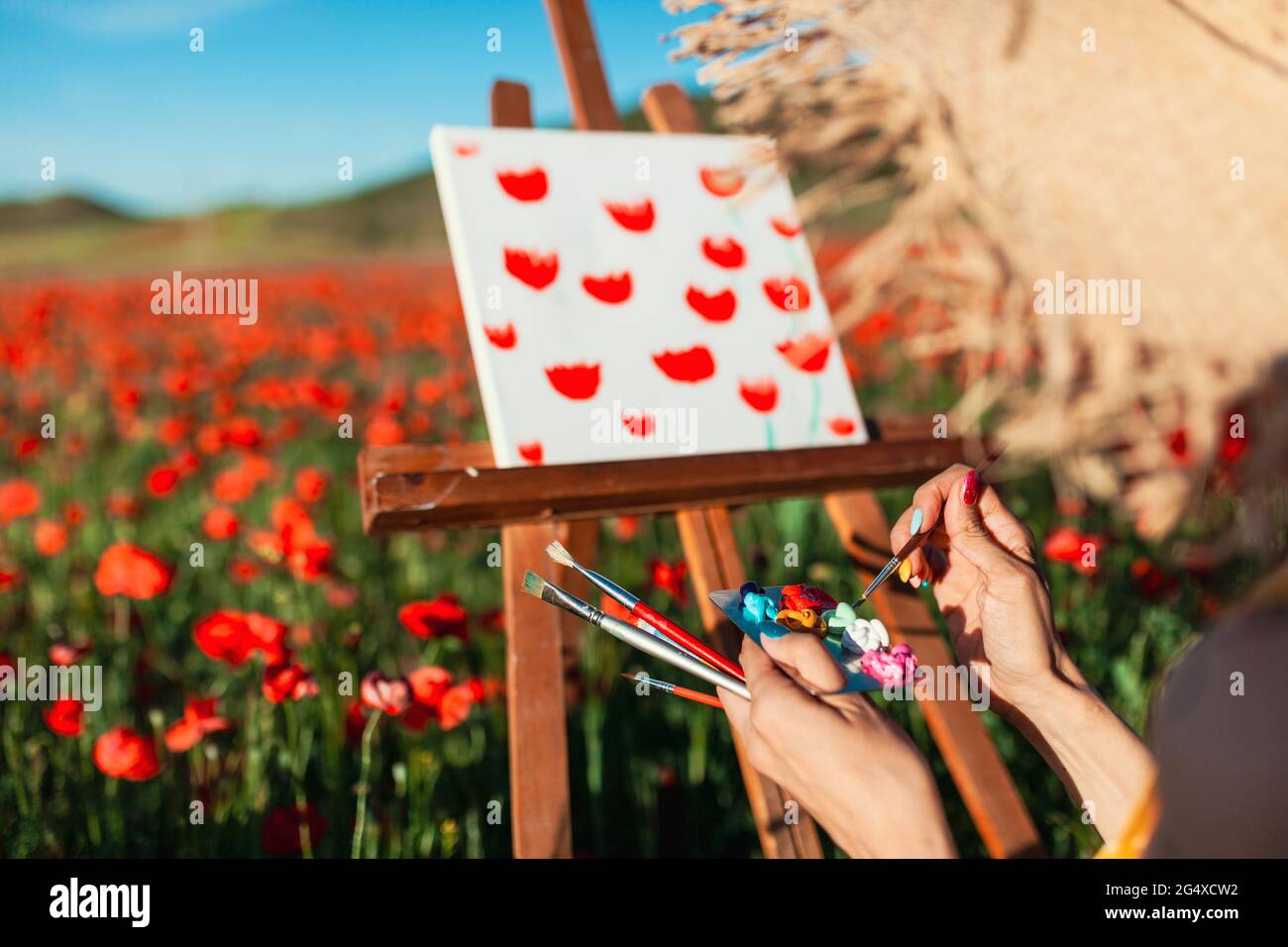 Female artist with paint on palette by canvas at poppy field Stock ...