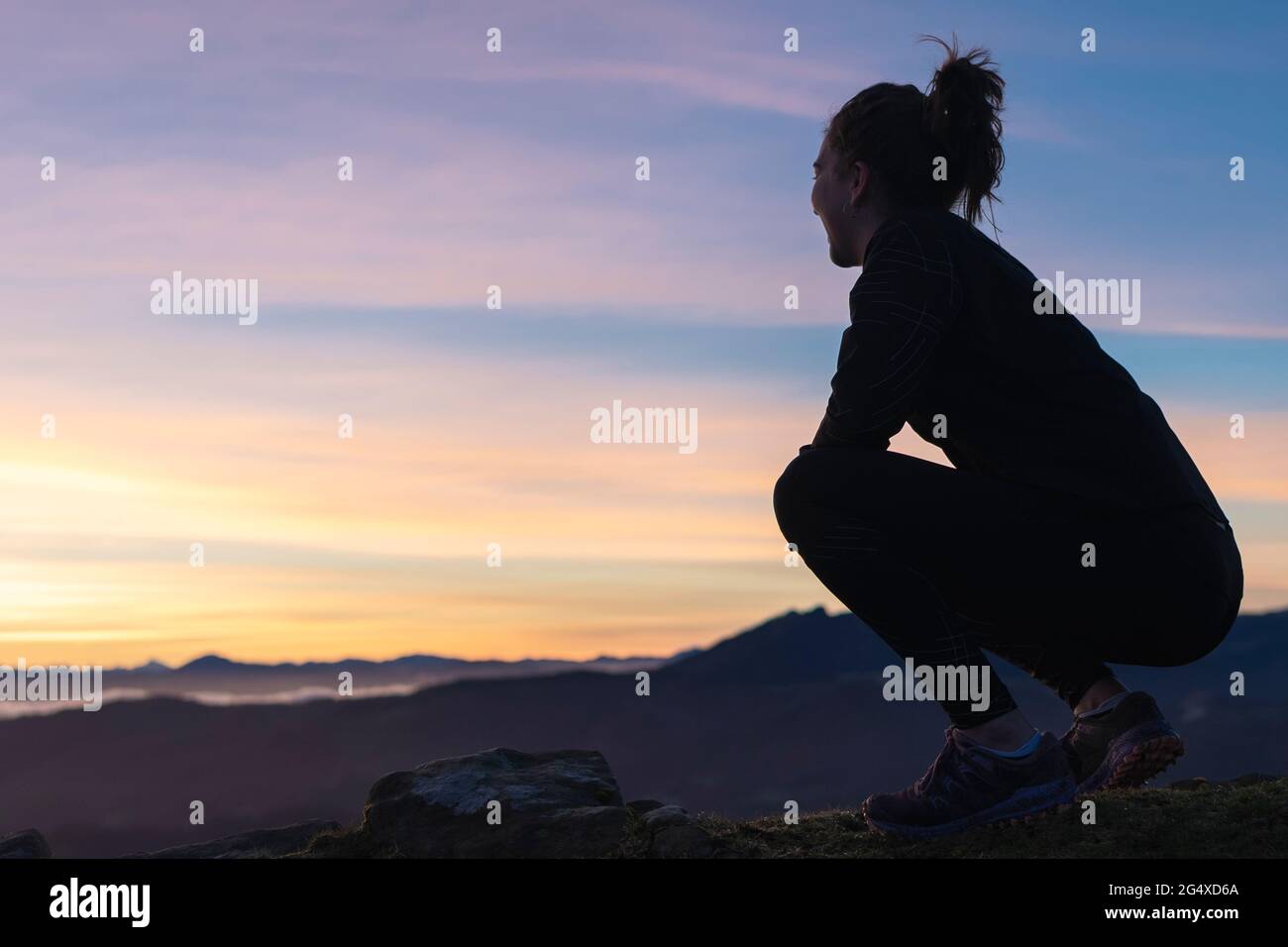 Young woman crouching on hill during sunrise Stock Photo - Alamy
