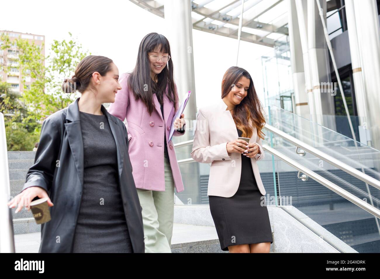 Smiling businesswomen with disposable coffee cup walking on staircase ...