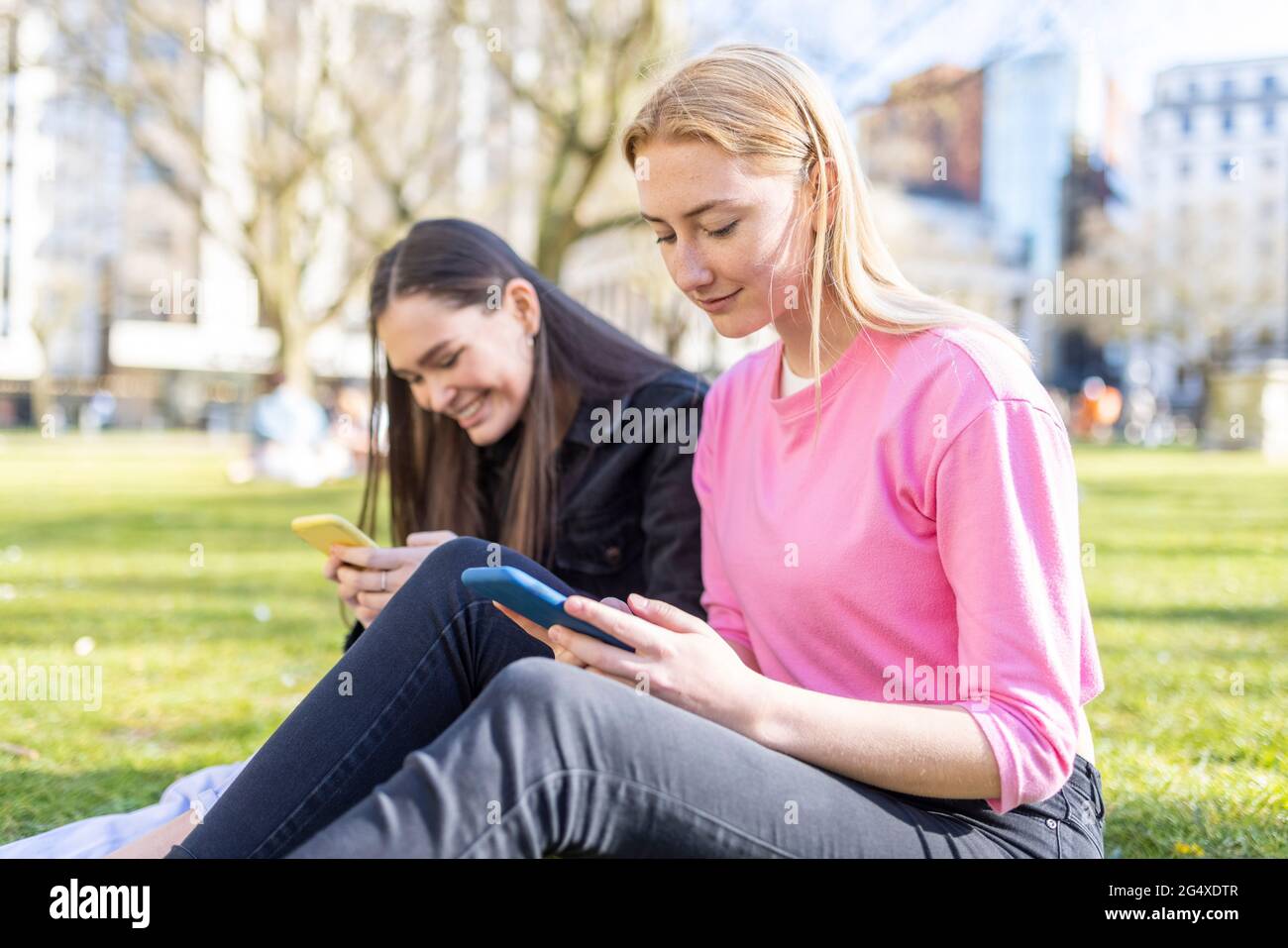 Female friends using mobile phone at public park Stock Photo - Alamy