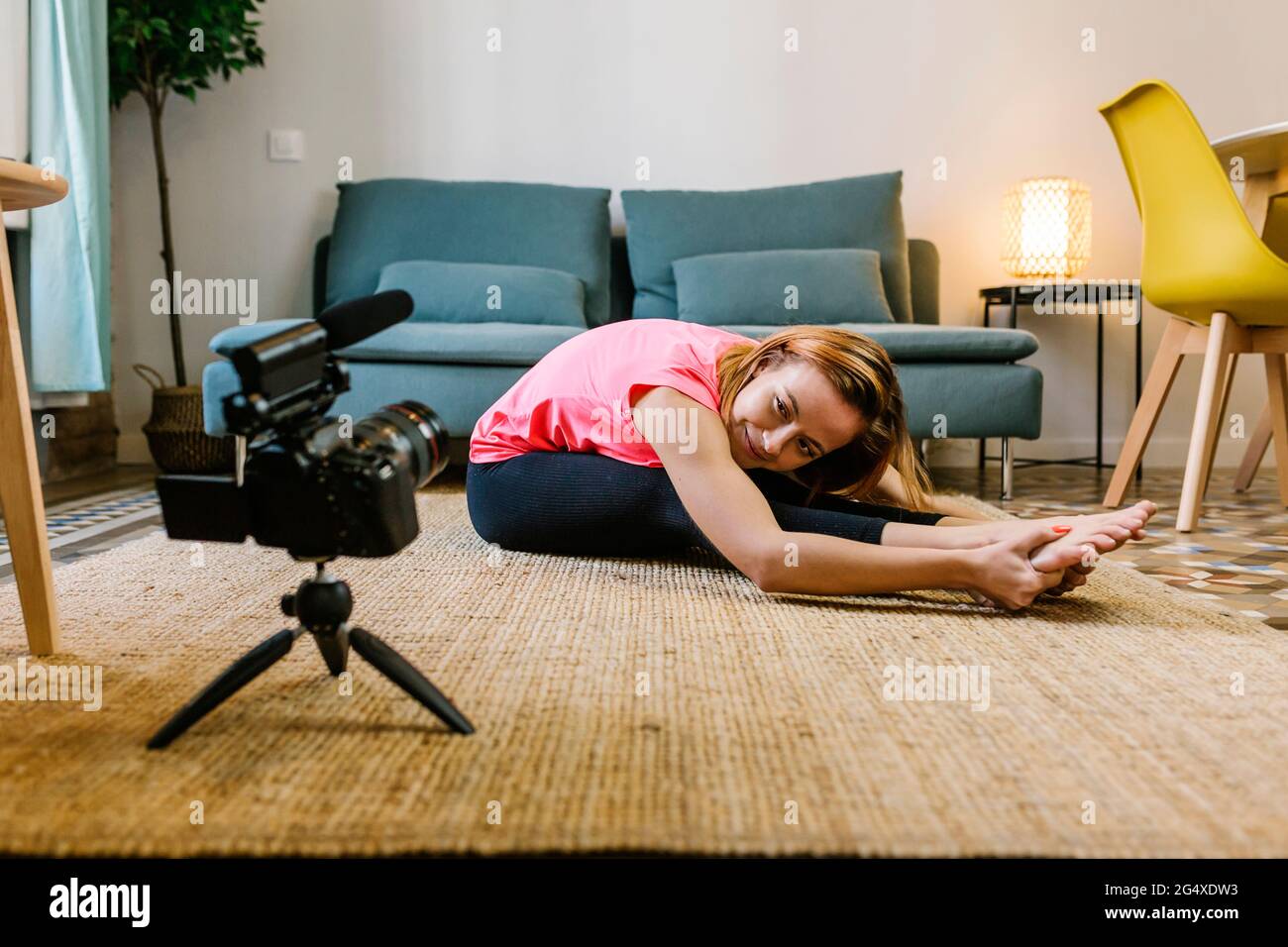 Female influencer vlogging while doing stretching exercise at home ...