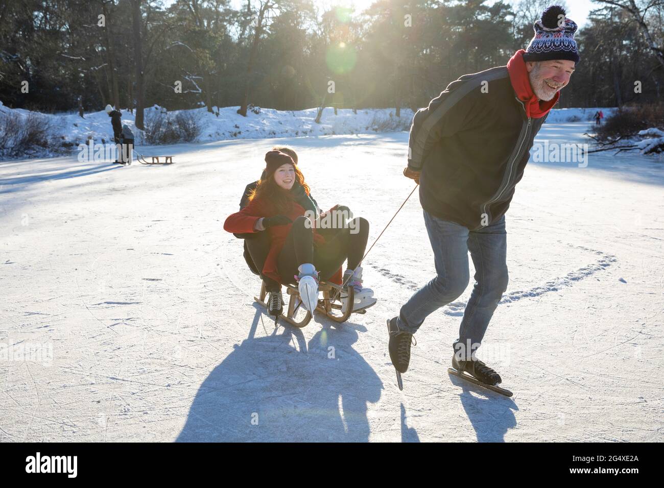 Senior man with young couple pulling on sled while ice skating over ...