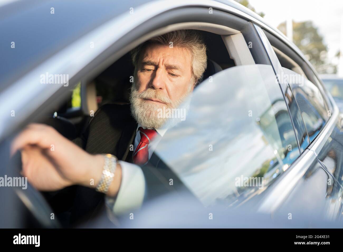 Mature businessman looking at wristwatch while driving car in city ...