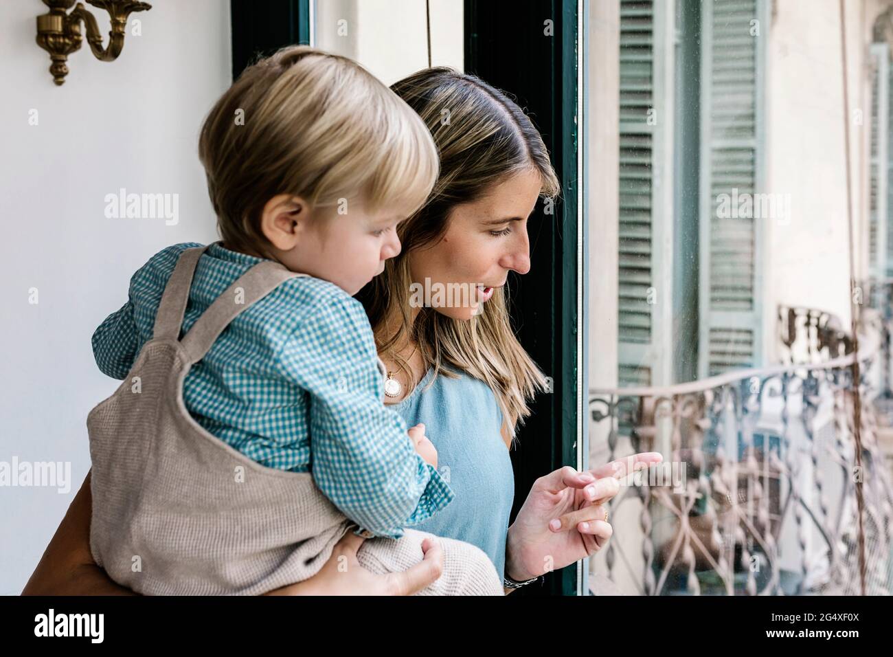 Woman carrying son while looking through window at home Stock Photo - Alamy