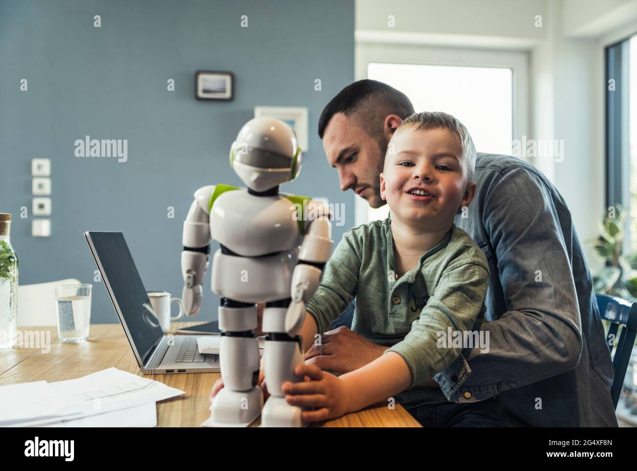 Smiling boy playing with robot while father working on laptop at home ...
