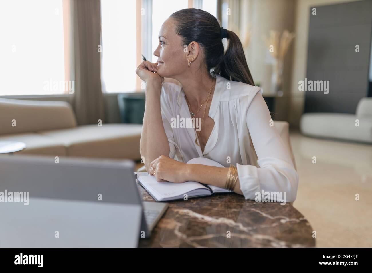 Thoughtful female professional sitting with diary at table in lobby ...