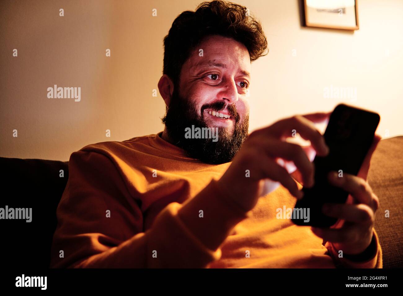 Smiling man using mobile phone while sitting on sofa at home Stock ...