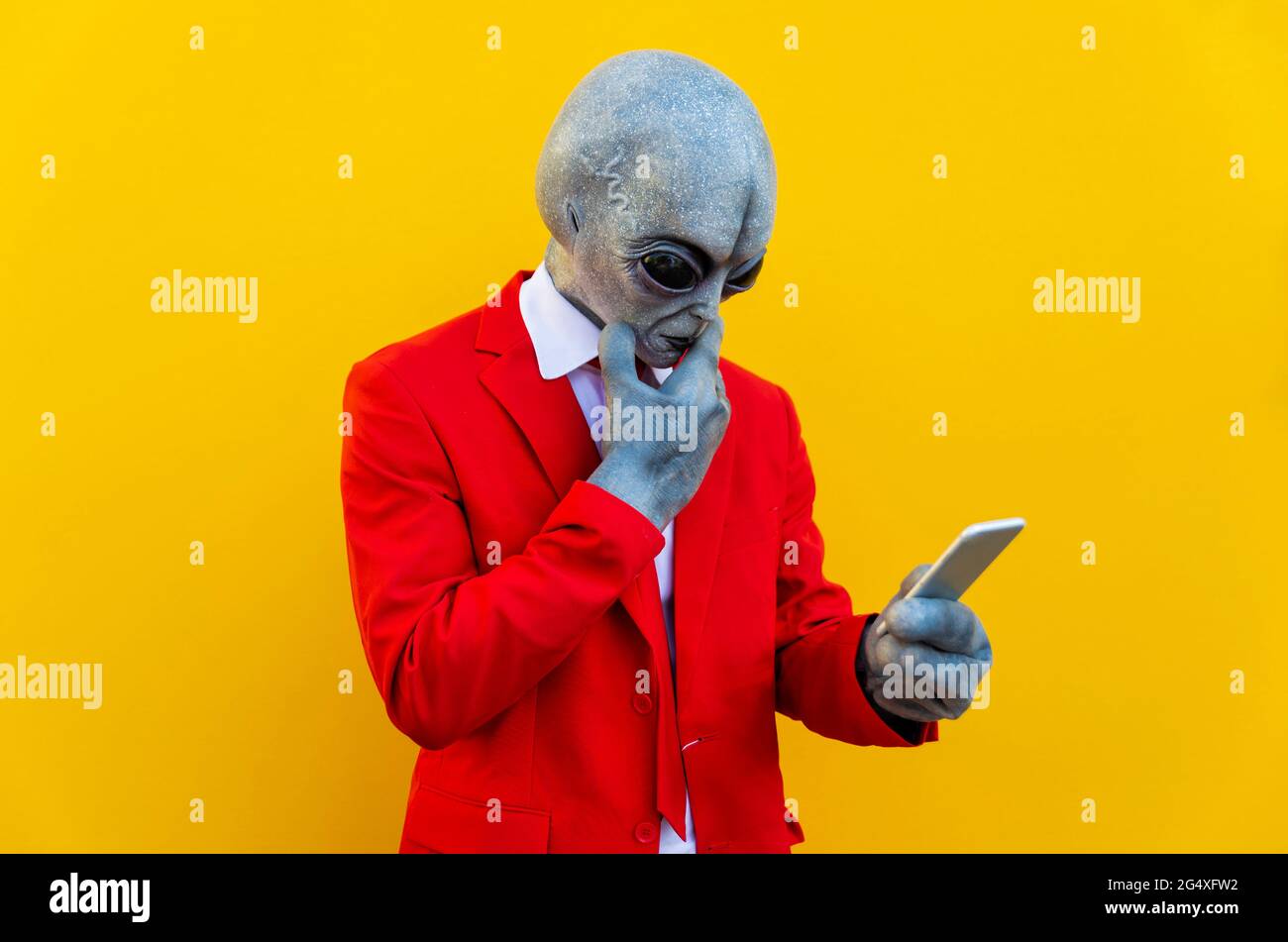Portrait of man wearing alien costume and bright red suit using smart ...