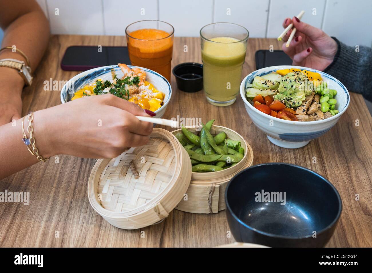 Female friends eating Chinese food with edamame beans in basket at ...