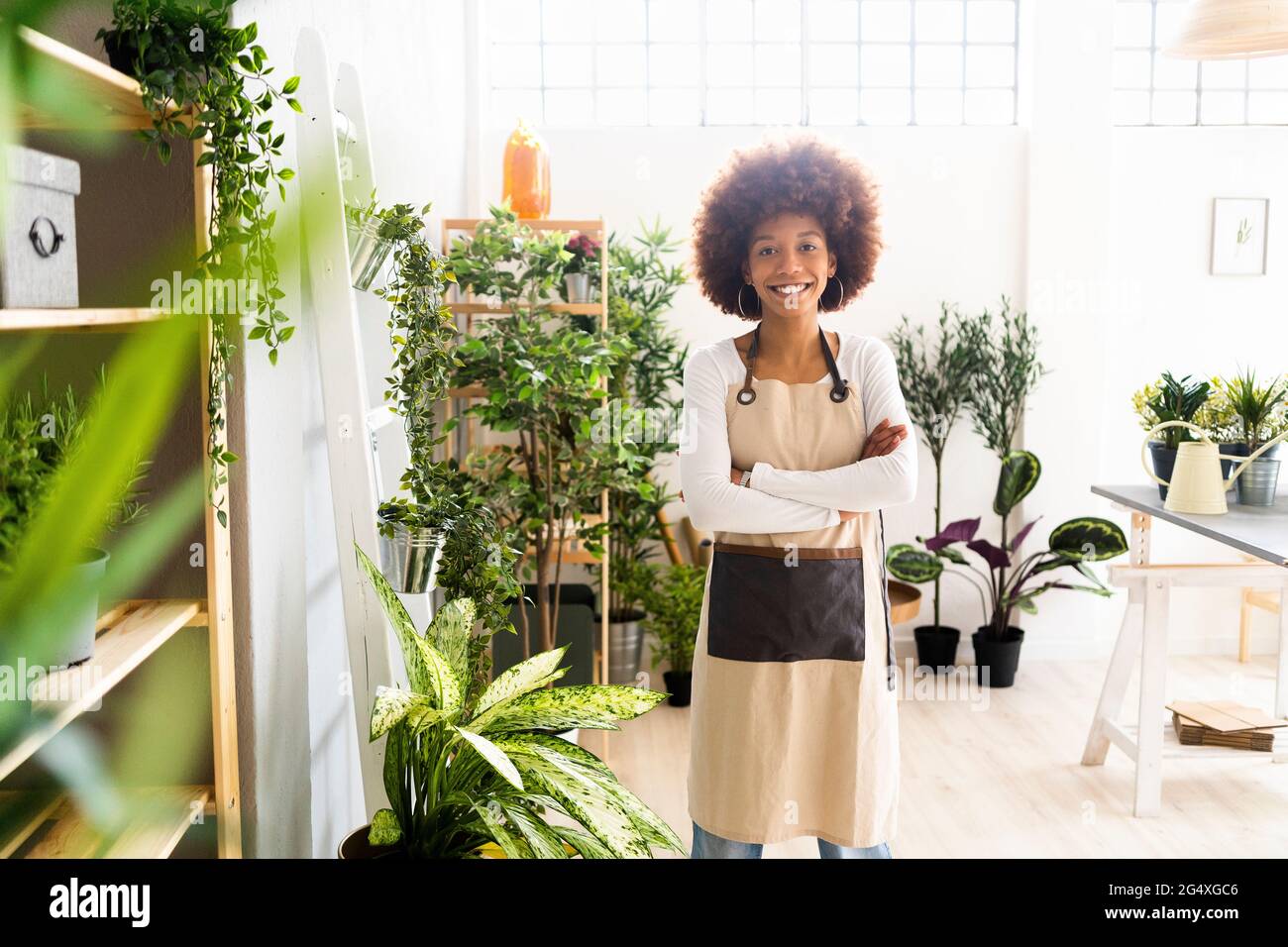 Confident female shop owner with arms crossed standing at plant store ...