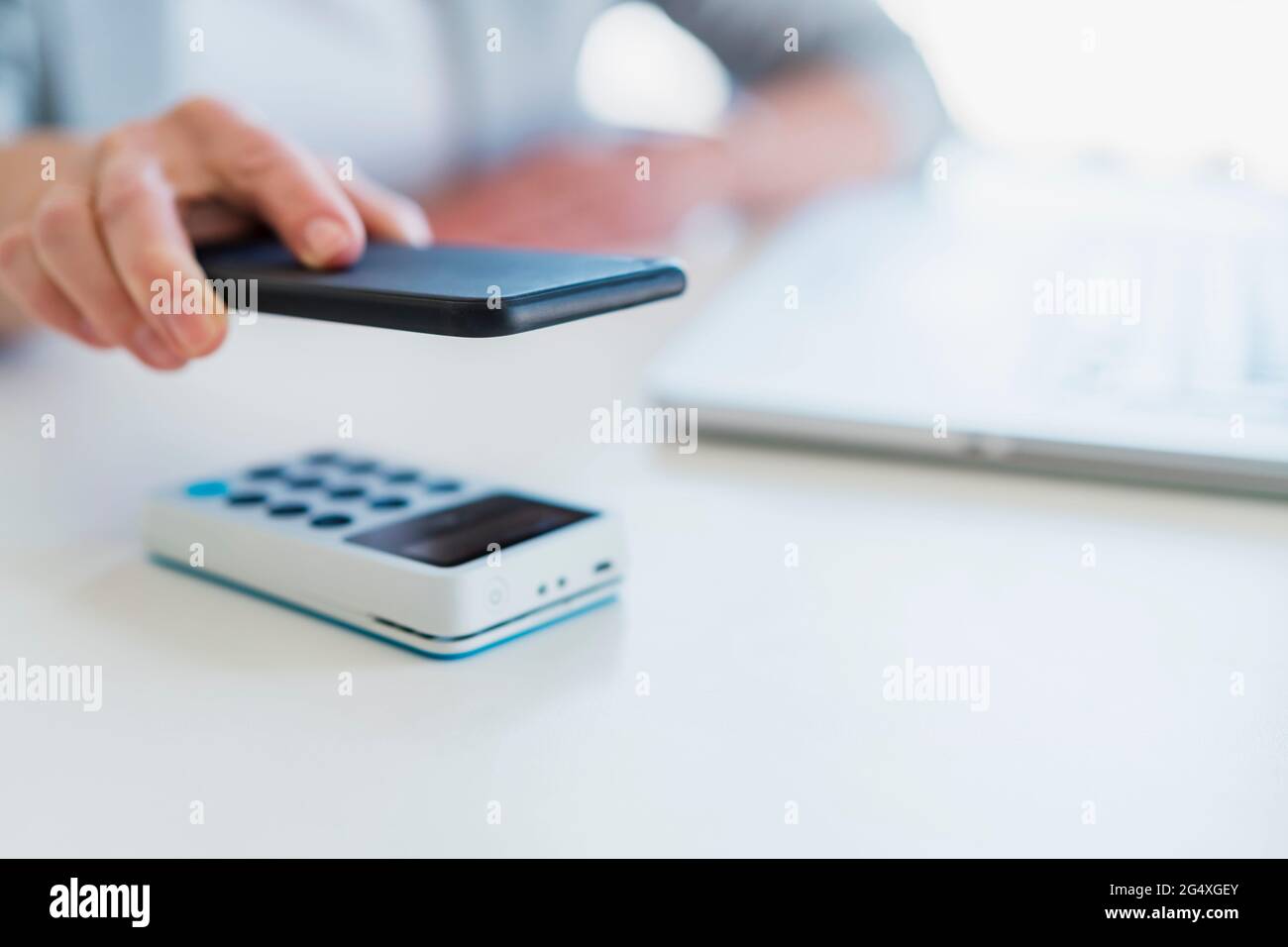 Businesswoman scanning QR code on mobile phone through card terminal at ...