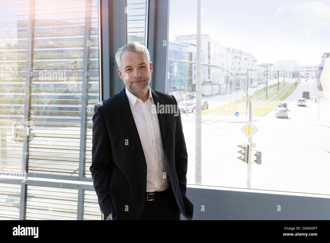 Male professional standing in front of glass window at office Stock ...