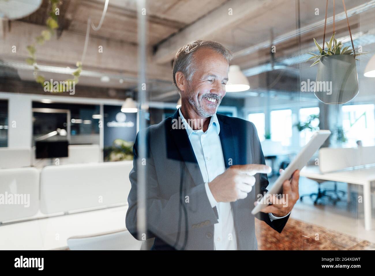 Smiling businessman using digital tablet behind glass wall Stock Photo ...