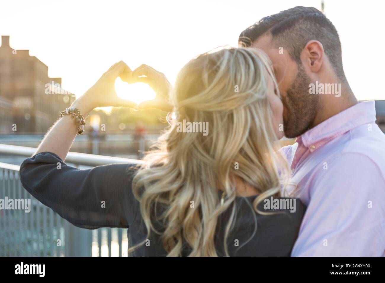 Romantic couple kissing each other while making heart shape with hands ...