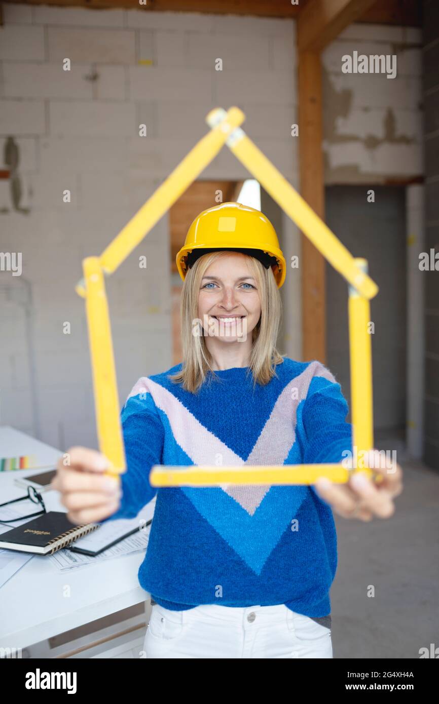 Smiling female architect looking through house shaped folded ruler at ...