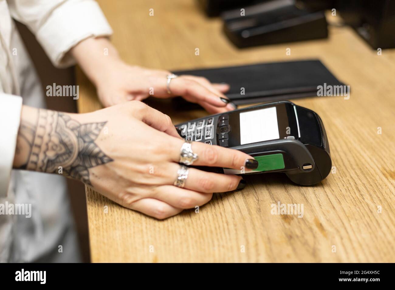 Young tattooed female cashier using credit card reader at checkout in ...