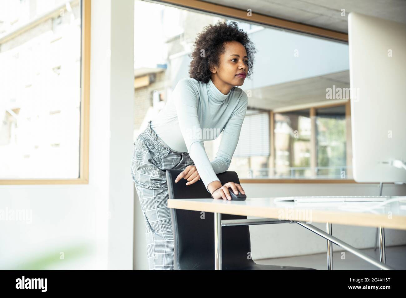 Female professional using computer while leaning on chair at office ...