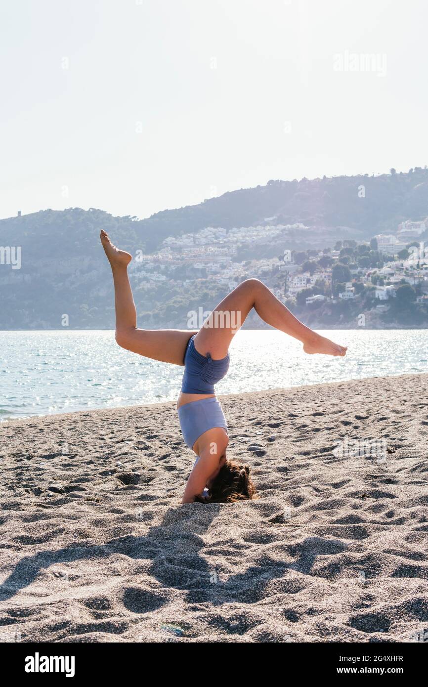 Mid adult woman practicing headstand on beach during sunny Stock Photo ...