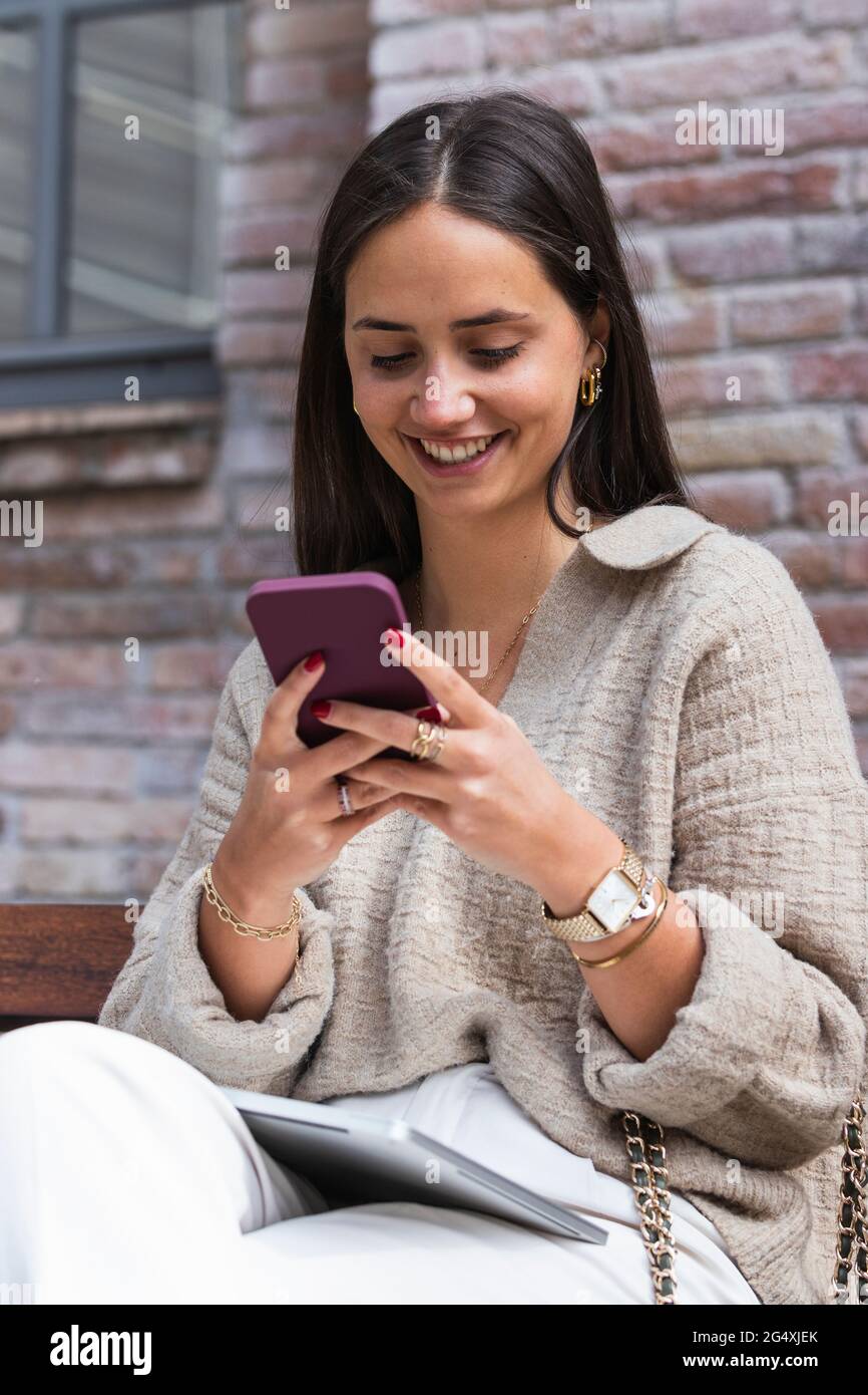 Smiling beautiful woman using mobile phone on bench Stock Photo - Alamy