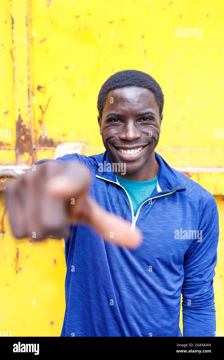 Smiling man pointing while standing in front of yellow wall Stock Photo ...