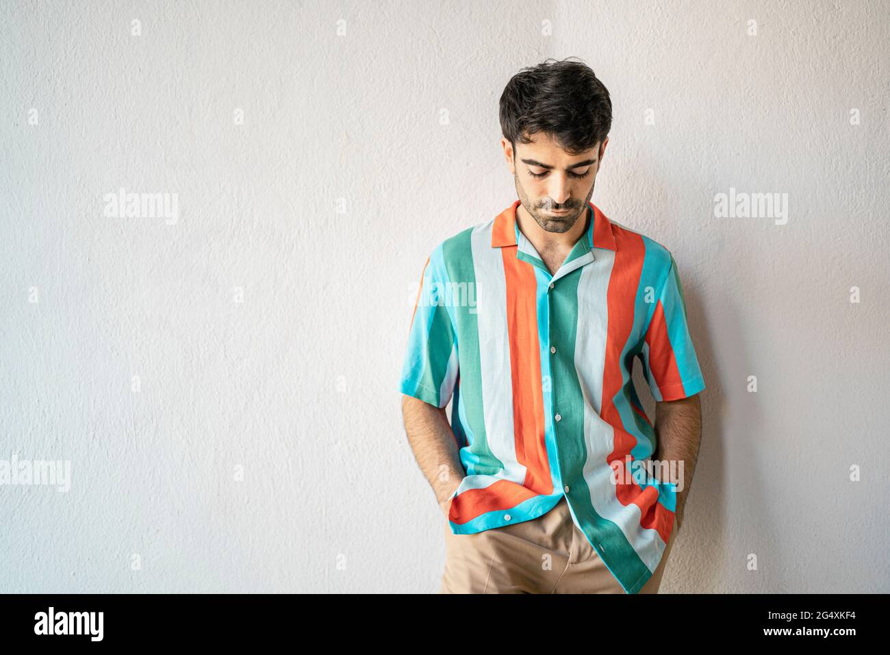 Young man with hands in pockets leaning on white wall Stock Photo - Alamy