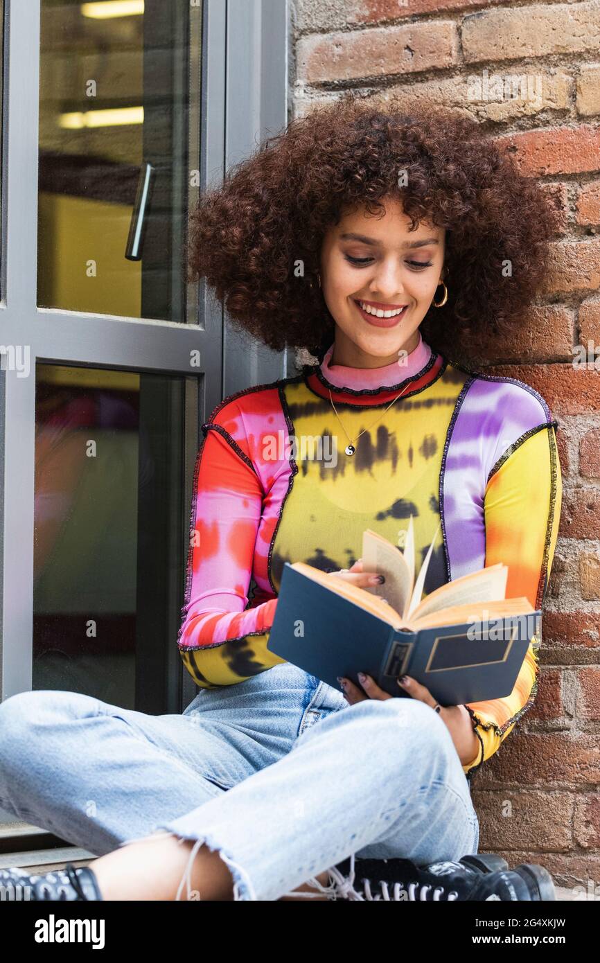 Student reading book while sitting on window Stock Photo - Alamy