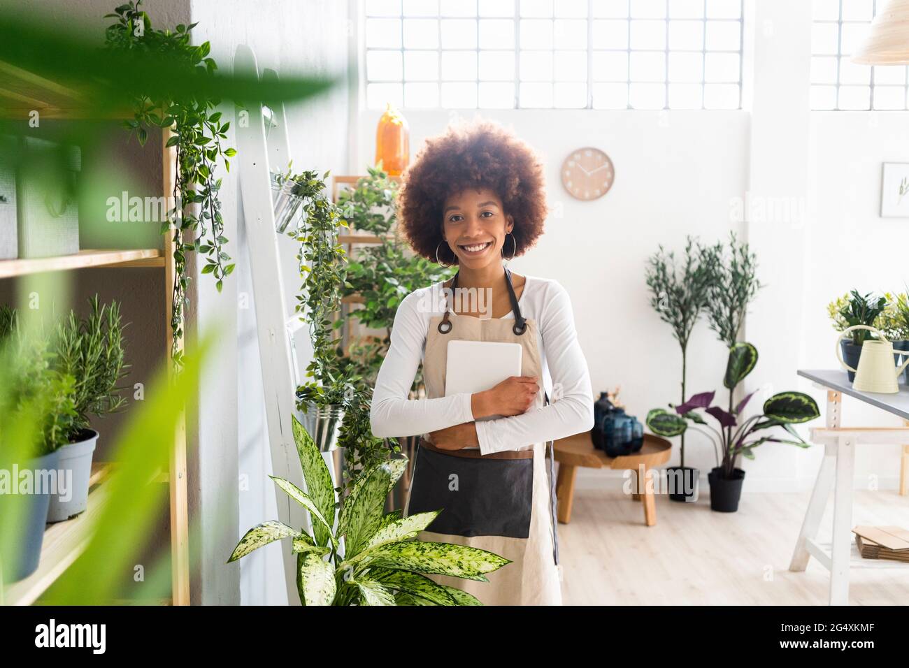 Female shop owner with digital tablet smiling while standing at plant ...