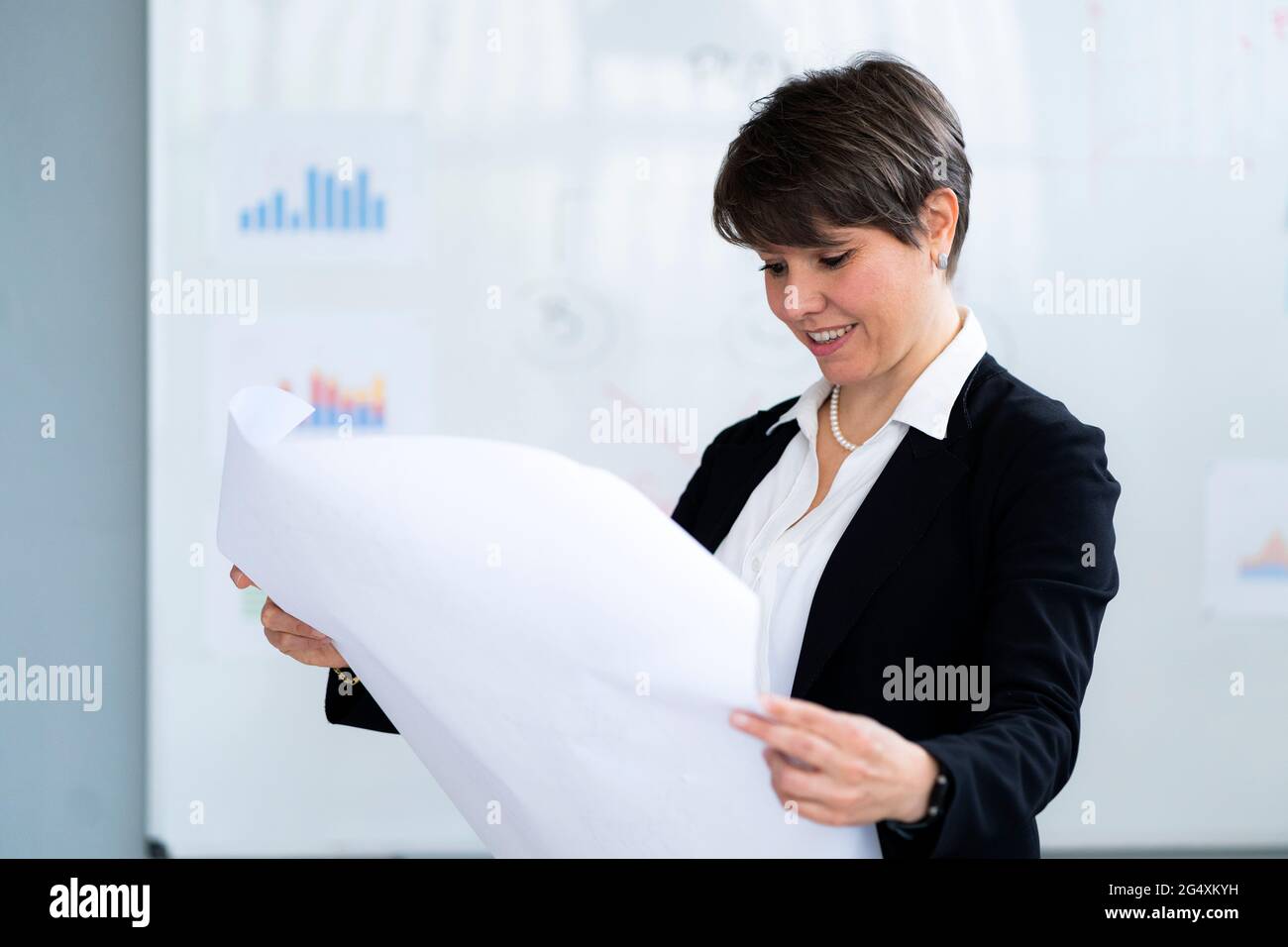 Smiling female professional analyzing paper chart while working in ...