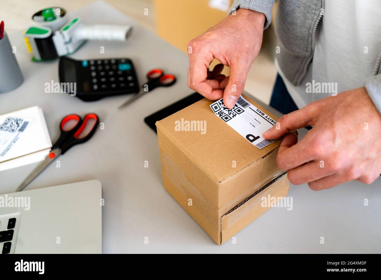 Male entrepreneur sticking QR code on cardboard package at desk Stock ...