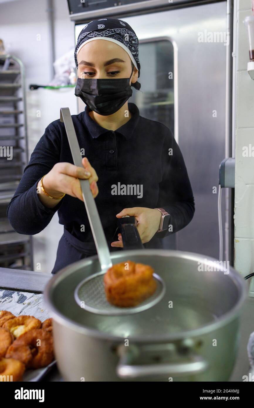 Female baker frying doughnut at commercial kitchen in bakery Stock ...