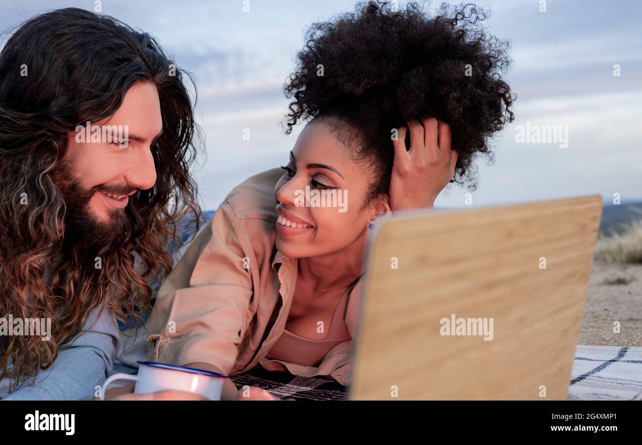 Smiling boyfriend looking at girlfriend lying by laptop Stock Photo - Alamy