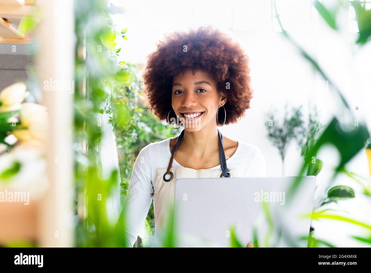 Female shop owner with laptop smiling at plant store Stock Photo - Alamy