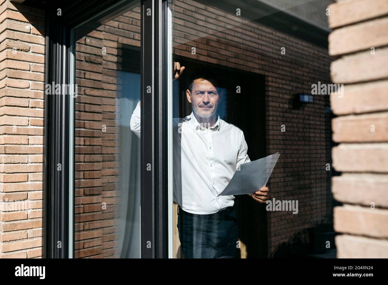 Businessman with documents seen through glass window of house Stock ...