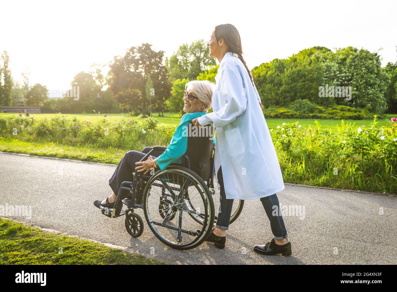 Female caretaker wheeling senior woman in wheelchair in park Stock ...
