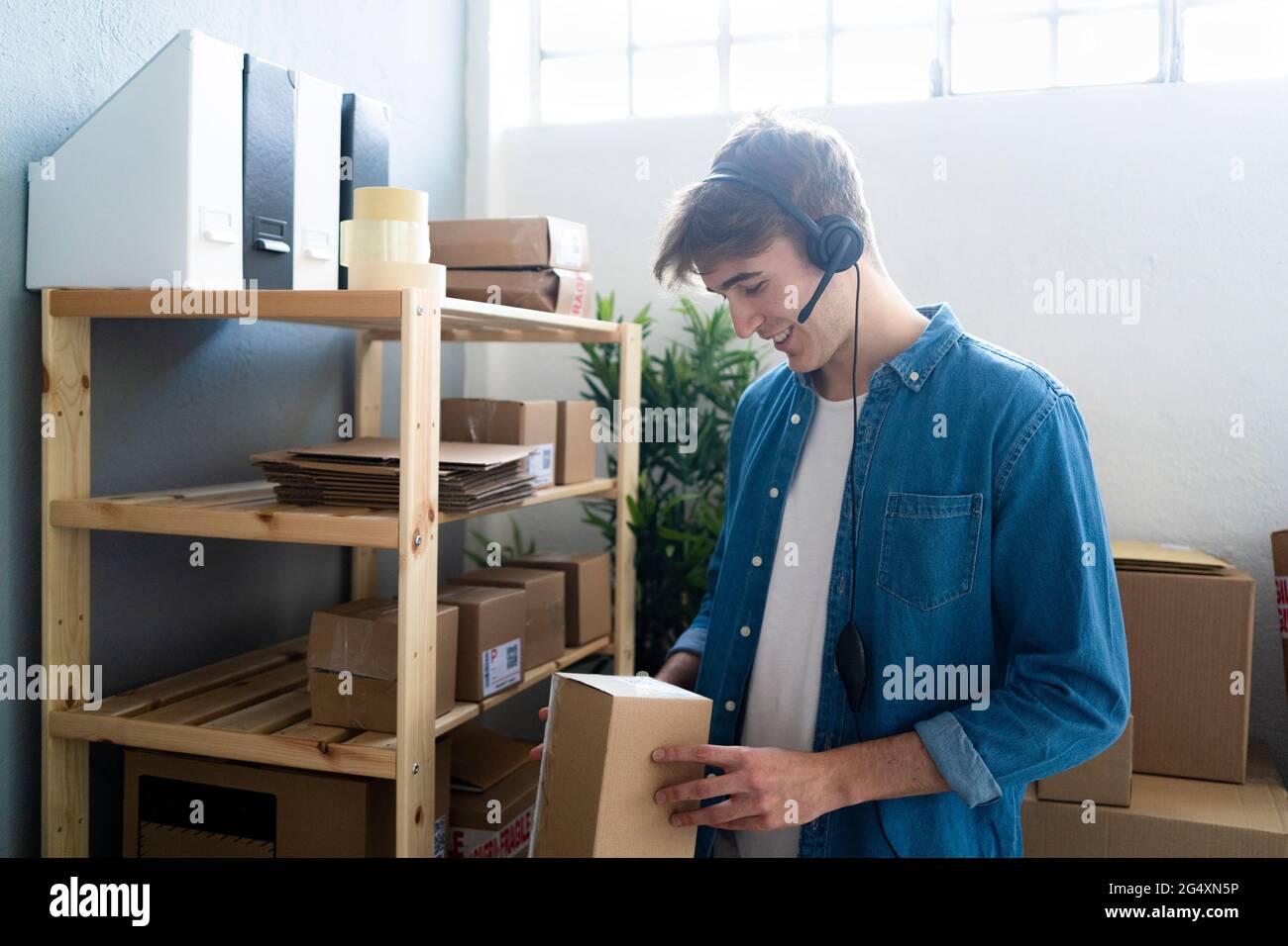 Smiling male customer service representative checking box by rack in ...