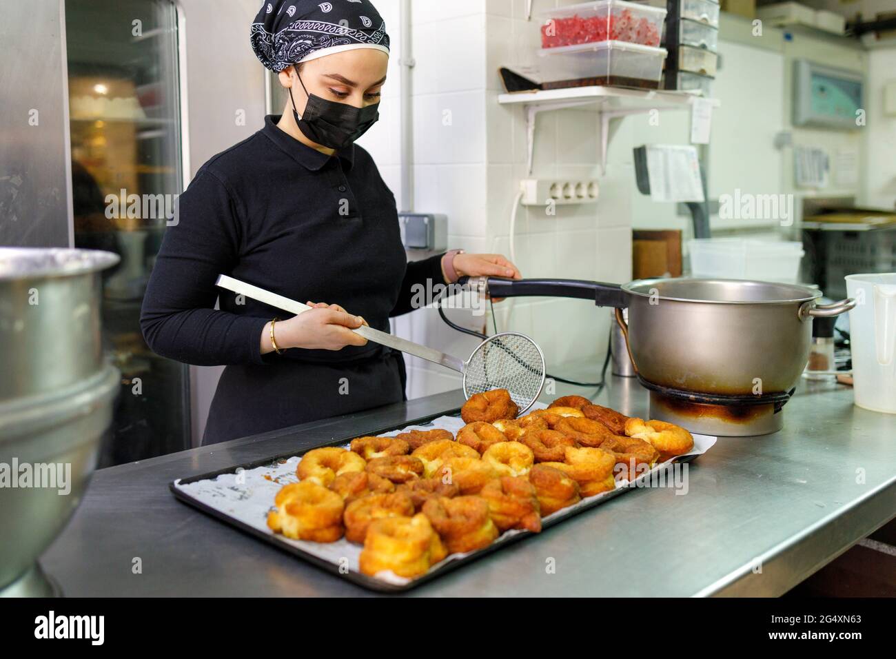 Female baker frying doughnuts in commercial kitchen at bakery Stock ...