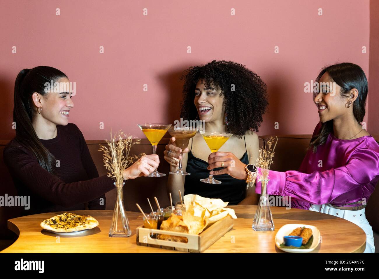 Young women toasting drinks while sitting at dining table Stock Photo ...