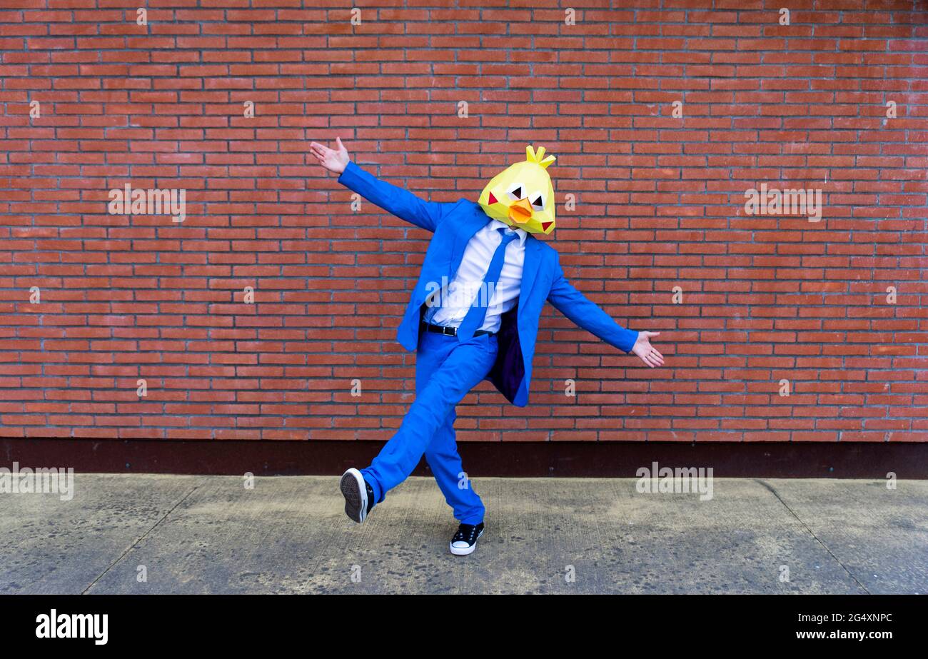 Man wearing vibrant blue suit and bird mask posing on one leg in front ...