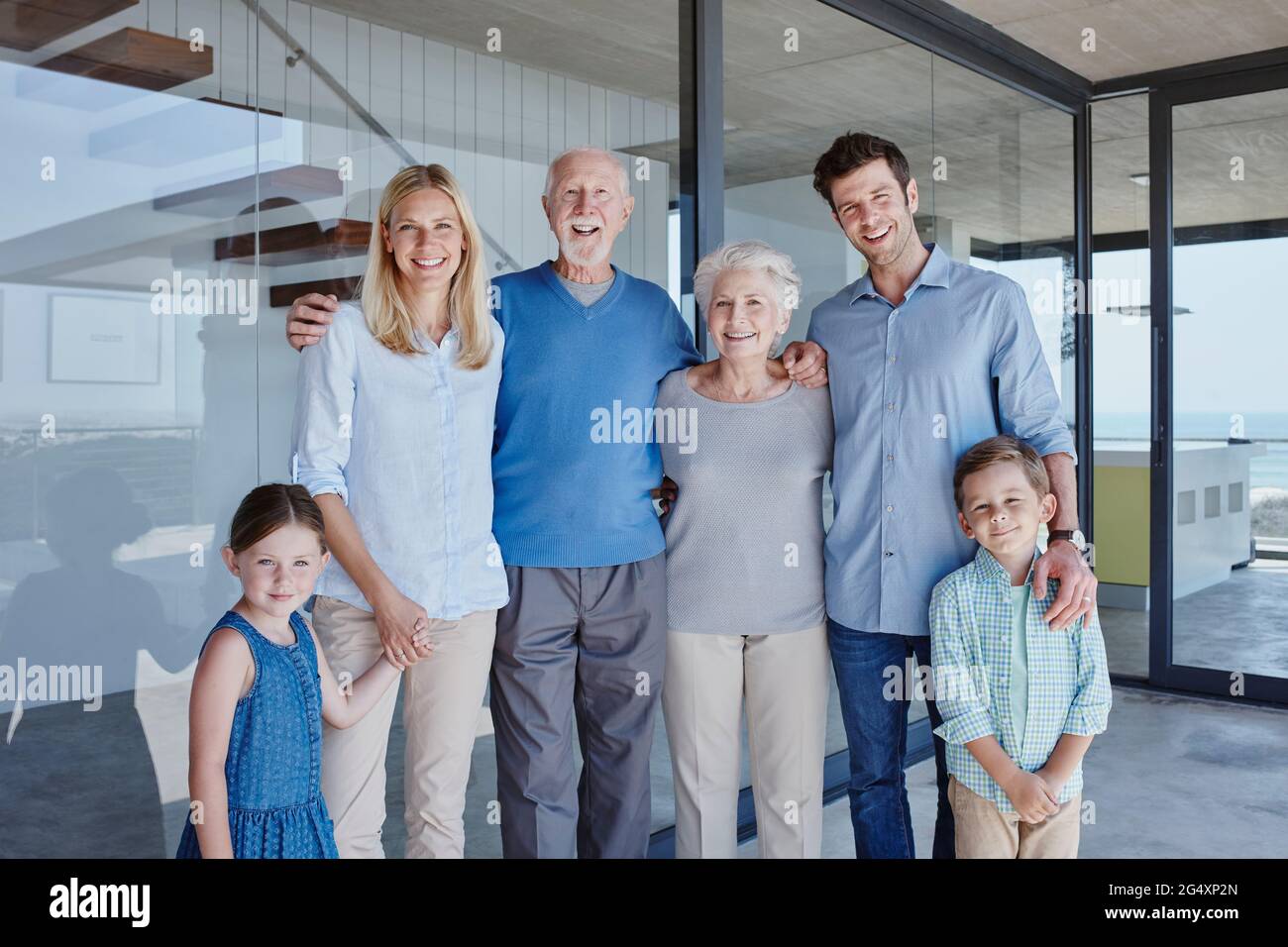 Happy multi-generation family standing together in front of glass wall ...