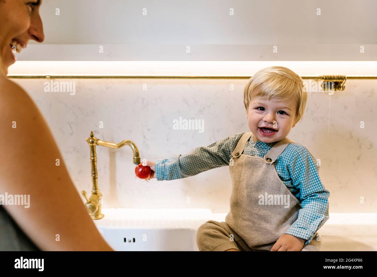 Cute baby boy washing fruit by smiling mother in kitchen at home Stock ...