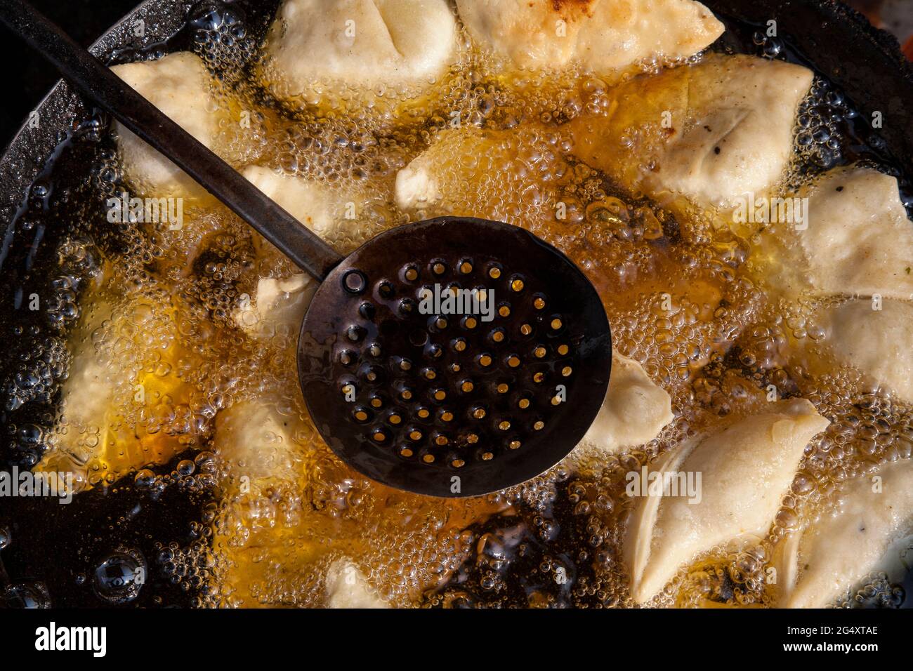 Samosas frying in oil using a traditional karahi at a street vendor's ...