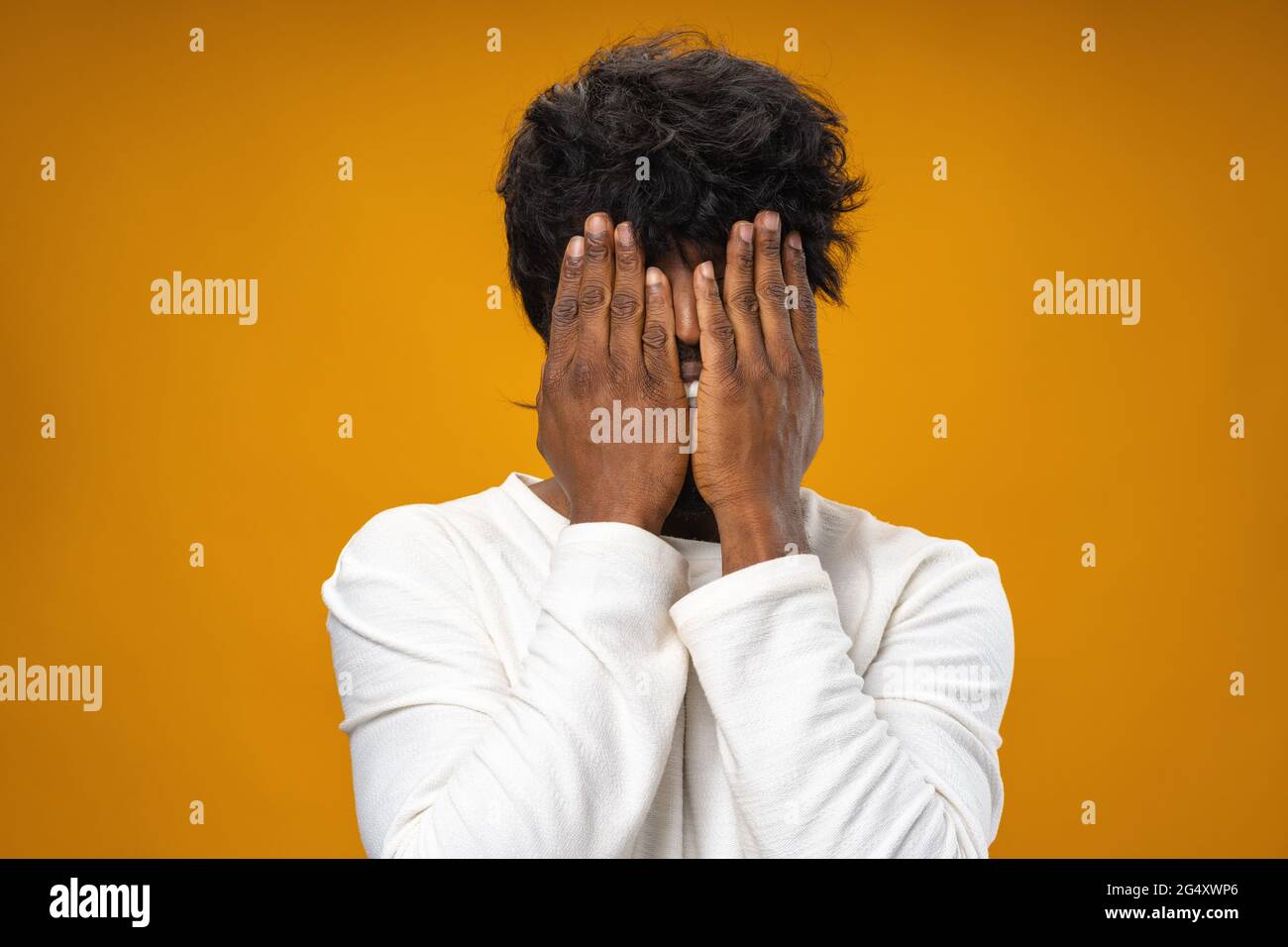 Black man closing face with hands against yellow background Stock Photo ...