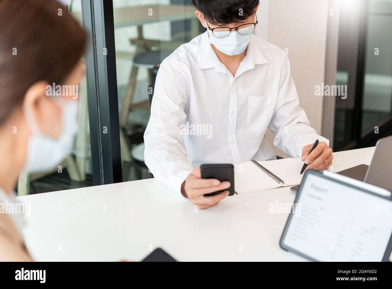 Two colleagues wearing surgical masks analyzing the data in chart for ...