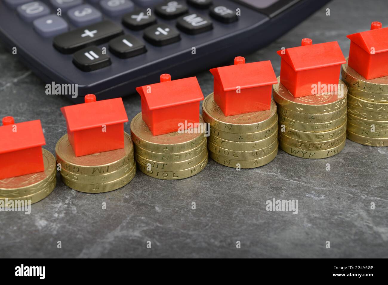 Toy houses on rising stacks of coins, with a calculator in the ...