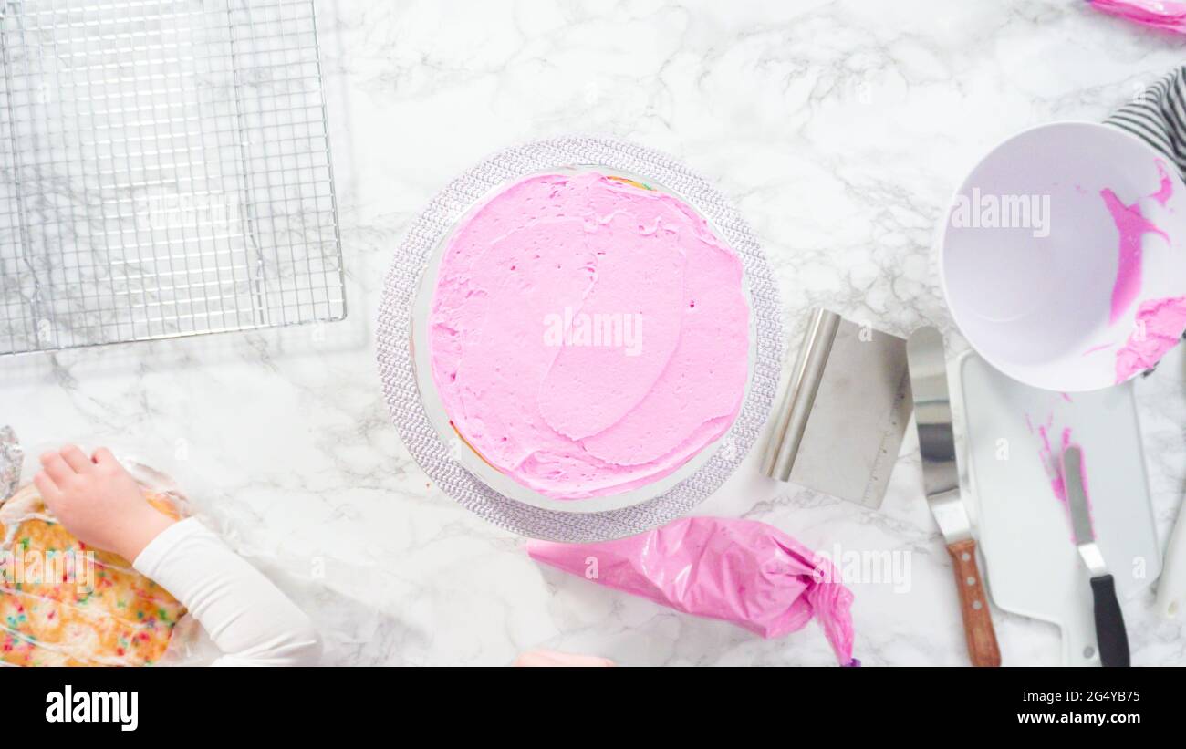 Flat lay. Step by step. Frosting round funfetti cake layers with pink ...