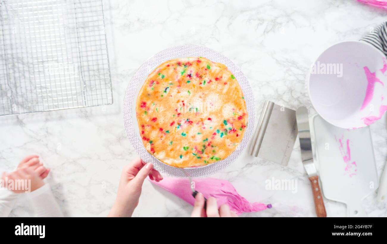Flat lay. Step by step. Frosting round funfetti cake layers with pink ...