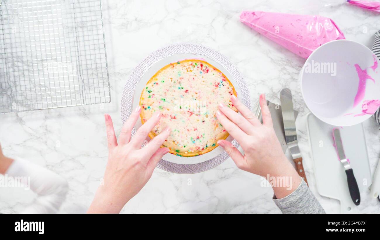Flat lay. Step by step. Frosting round funfetti cake layers with pink ...